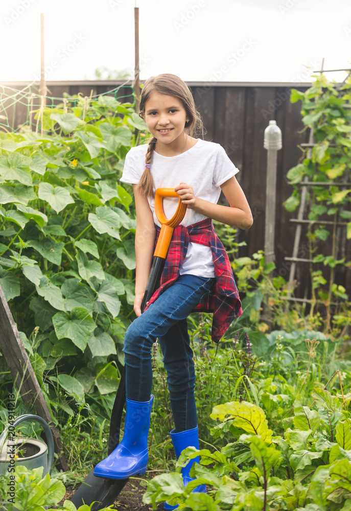 Toned photo of beautiful teenage girl digging soil in garden with spade ...