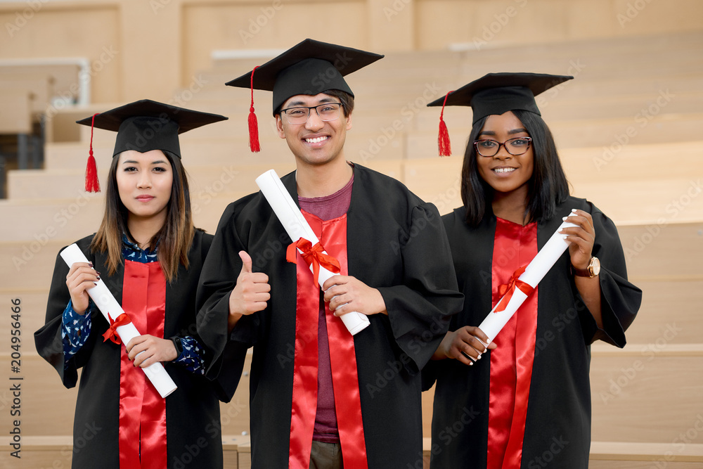 Smiling different nationalities graduates keeping diplomas standing in ...