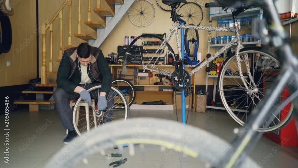Handsome mechanic is fixing back wheel with wrench while working in ...