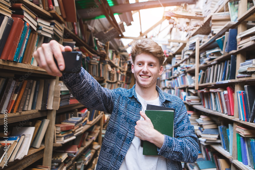 Handsome young man standing in a library with books in his hands and ...