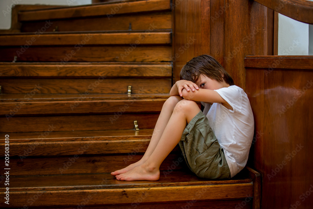 Sad child, sitting on a staircase in a big house, concept for bullying ...
