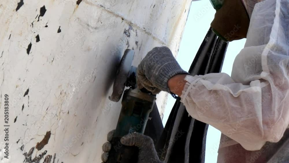 Workers tear off paint on metal in repairs process at shipyard. Working ...