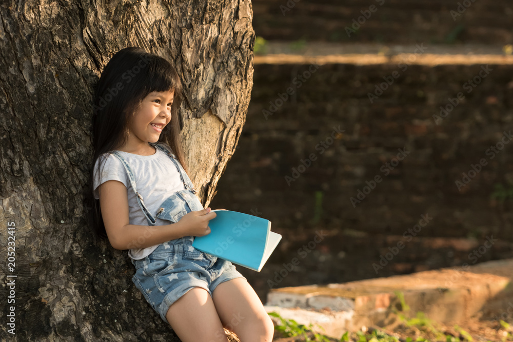 Little girl reading a book under big tree Stock Photo | Adobe Stock