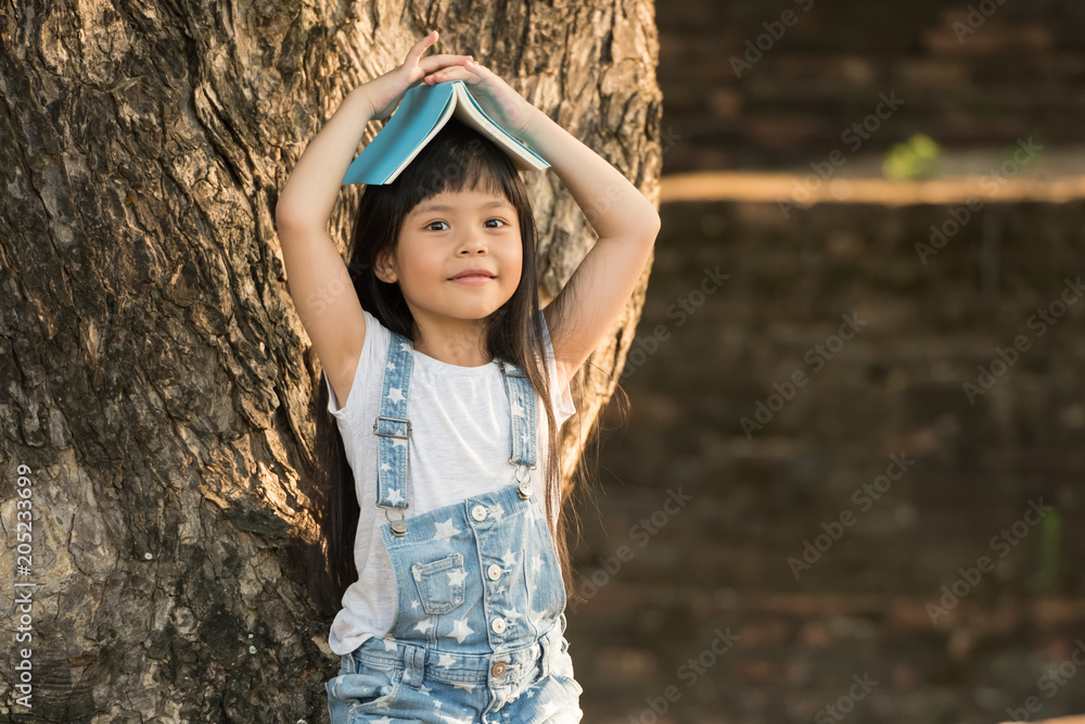 Little girl reading a book under big tree Stock Photo | Adobe Stock