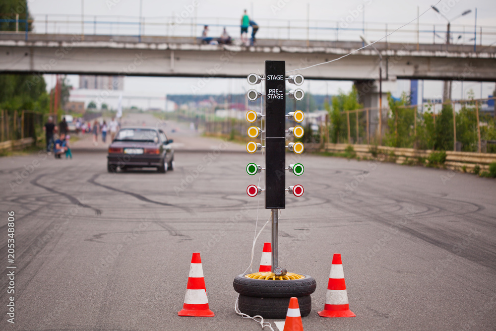 Traffic light at the start of a racing track with a car in the distance ...