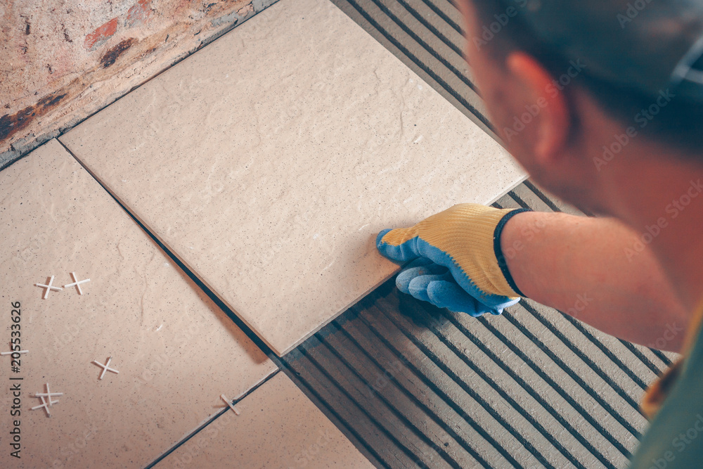 The worker carries out installation of a tile on a floor, finishing and ...