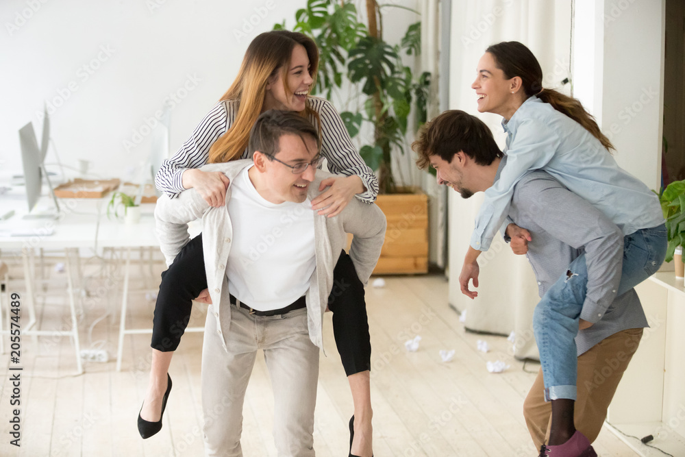 Happy colleagues having fun together enjoying piggyback ride in office ...