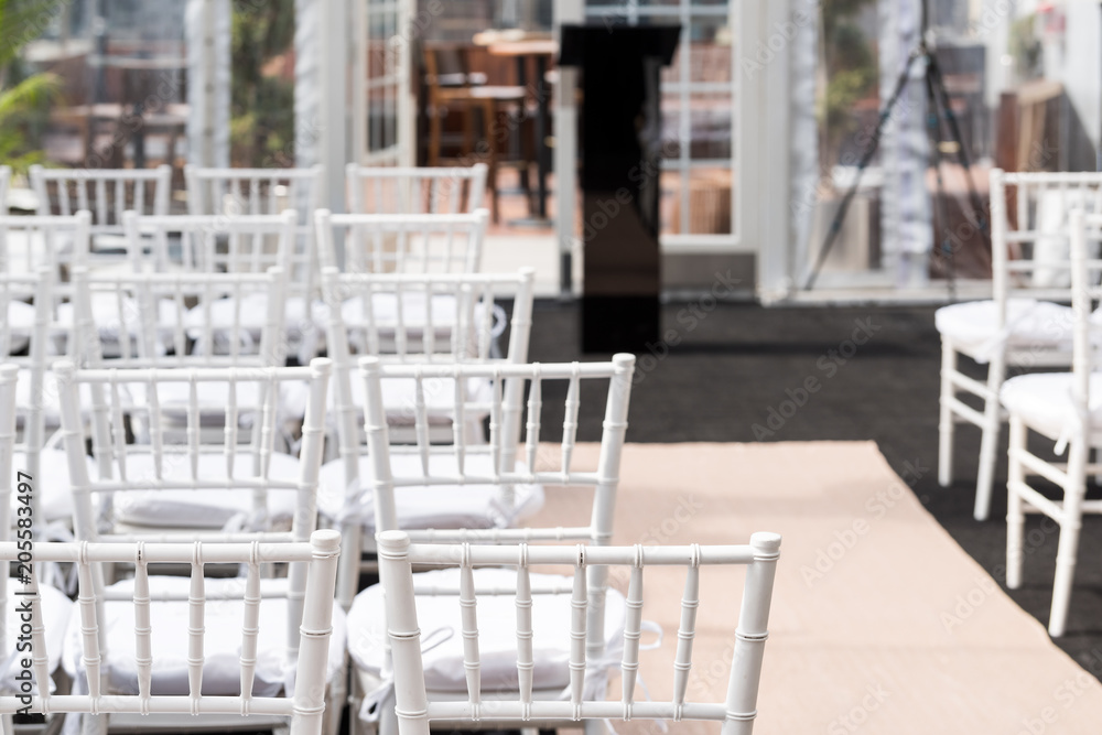 White wedding chairs for ceremony with background of rows of many seats ...