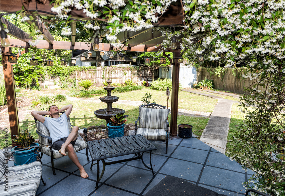 Young man lying down on patio lounge chair in outdoor spring flower ...