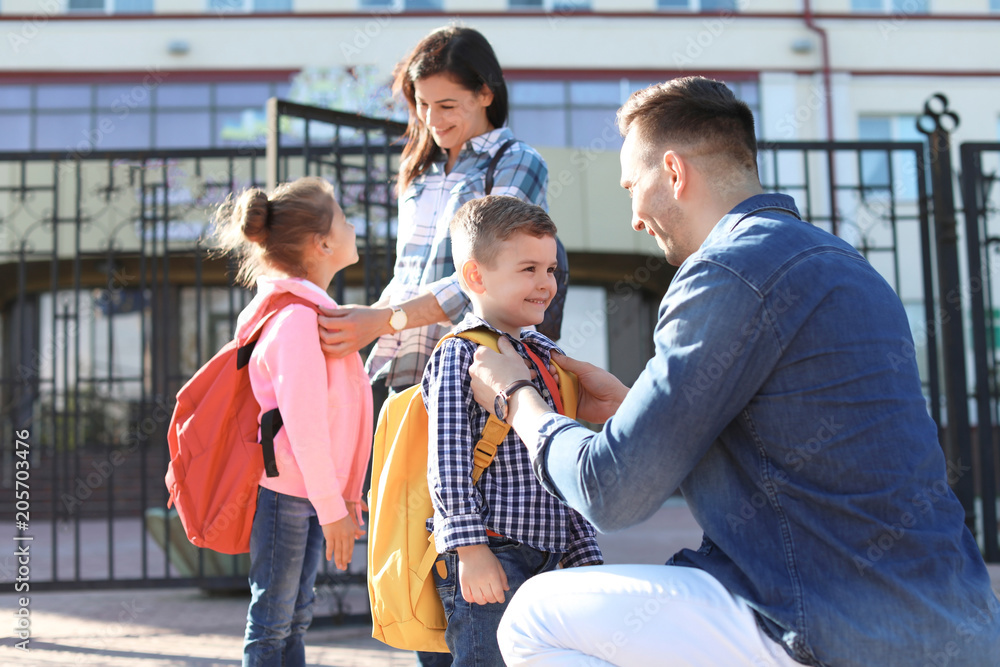 Young Parents Saying Goodbye To Their Little Children Near School Stock