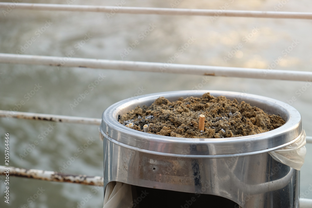 Cigarette stub buried in the pile of wet sand at top of metal trash bin ...