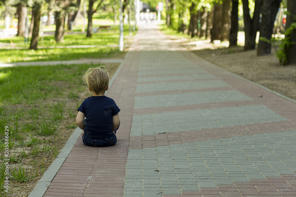 Little boy the kid in blue jeans sitting on the ground next in the ...
