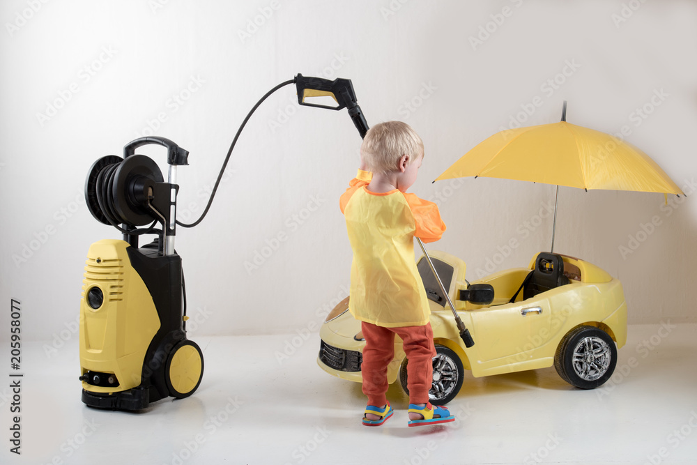 Happy child in yellow overalls and boots with high pressure washer ...