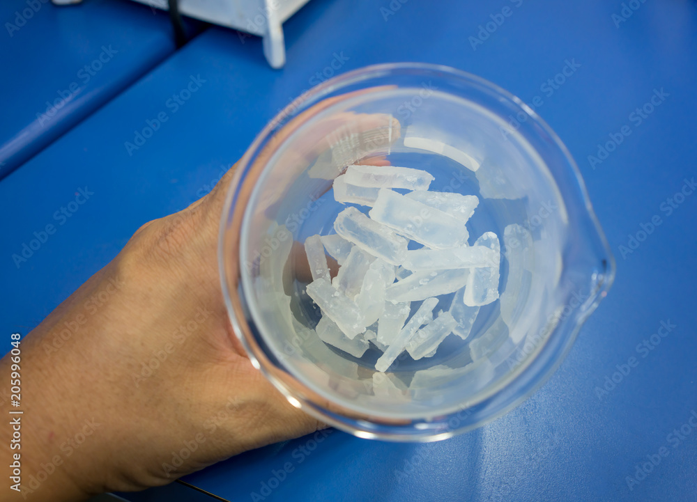 Hand holding a clear beaker containing with chemical ingredient on blue ...