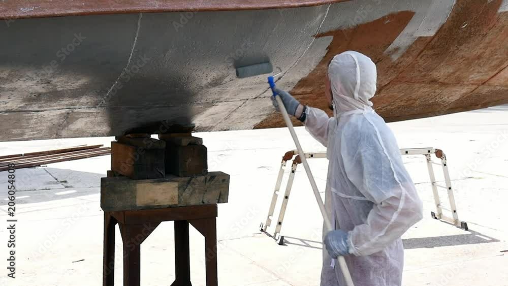 Worker paints metal of old rusty ship propeller at shipyard in port ...