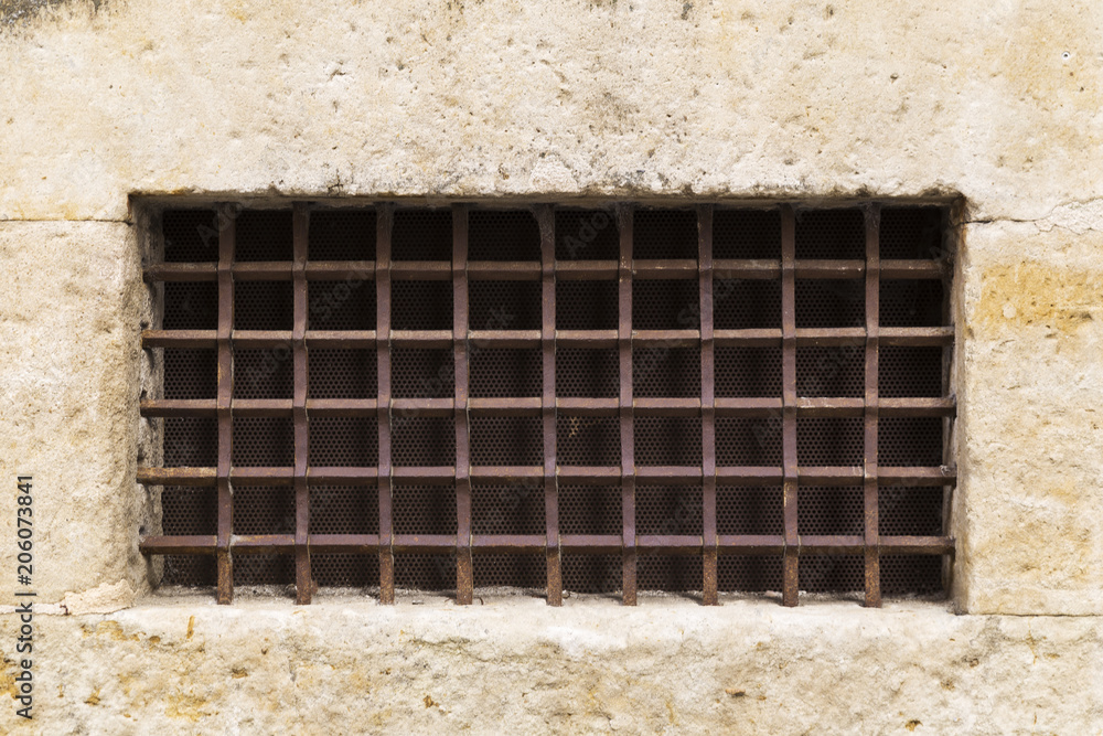 old window in a medieval castle protected by a rusty iron grating with ...