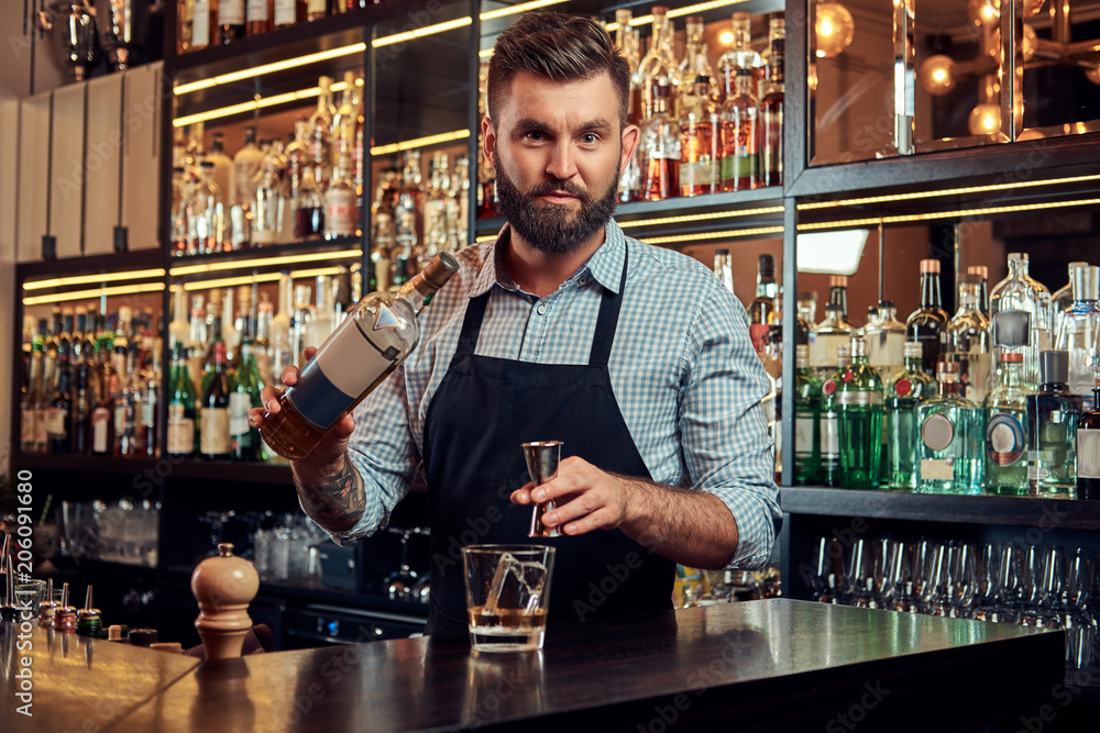 Stylish brutal barman in a shirt and apron makes a cocktail at bar ...