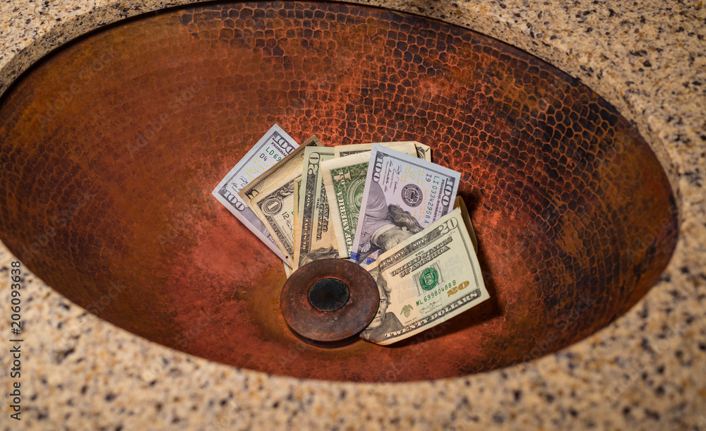 Concept. Wasting money down the drain. US currency, dollars, cash in a ...