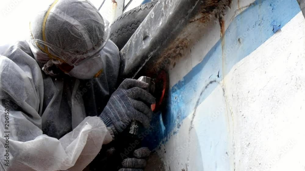Working people tear off paint on metal in repairs process at shipyard ...