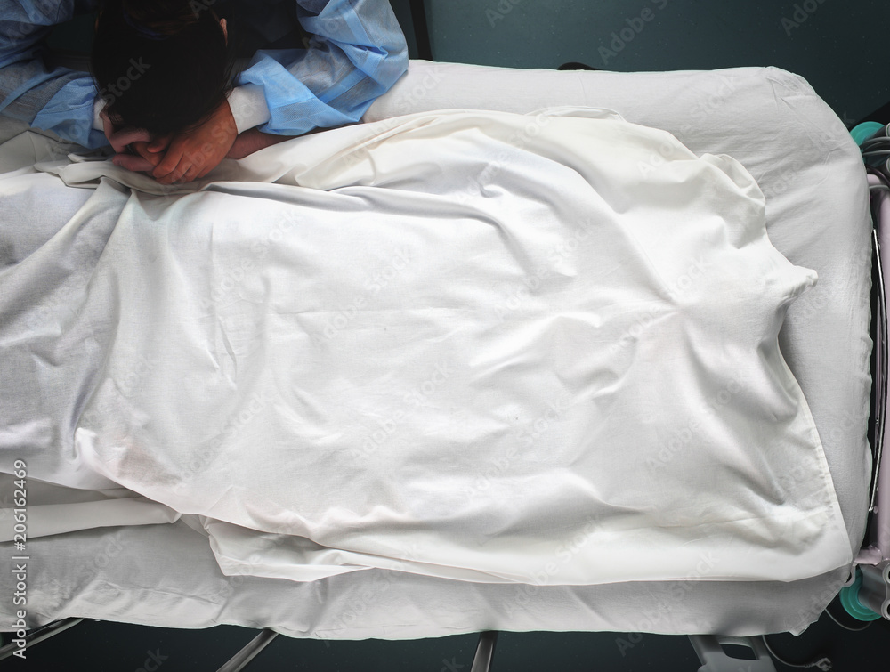 Crying woman hold the hand of dead man, covered with the white bed ...