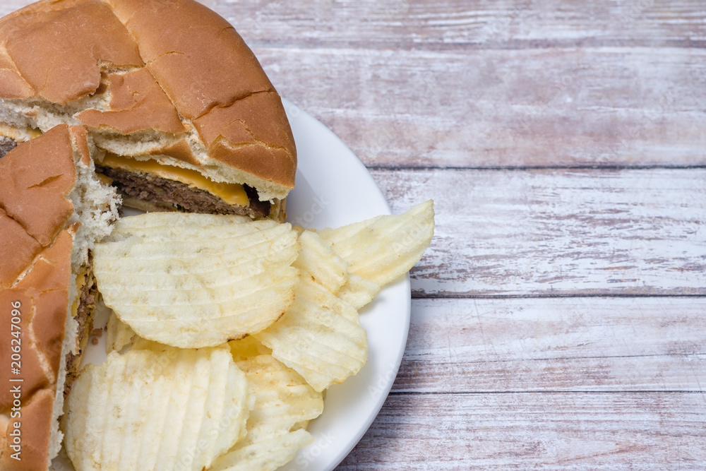 Cheeseburger and chips on white plate with wood table background and ...
