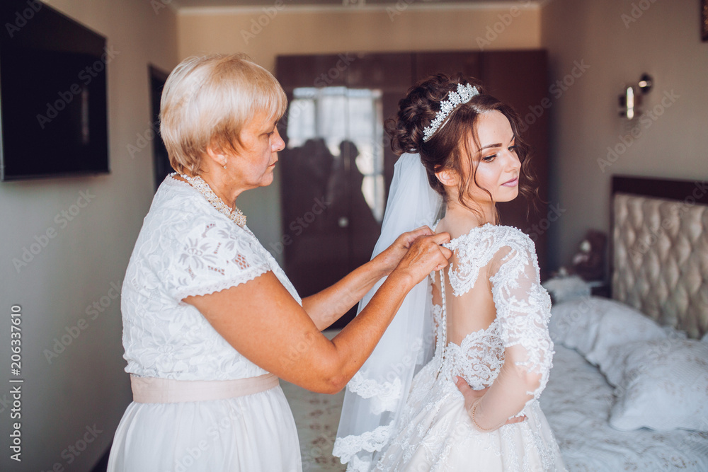 Beautiful bridesmaid and mother help put on wedding dress on gorgeous ...