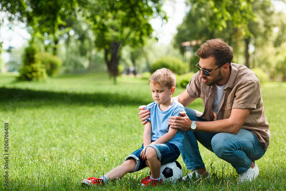 father hugging and supporting sad son after playing football at park ...