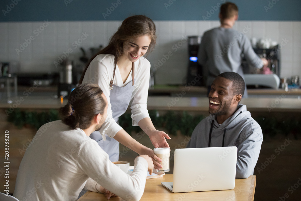 Smiling friendly waitress serving coffee drinks to diverse male friends ...