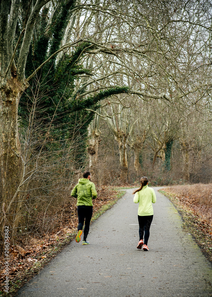 Rear view of young athletic couple running enthusiastically on a winter ...