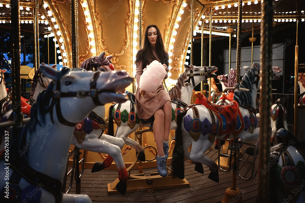 Young beauty model woman posing with old horse carousel in summer park ...
