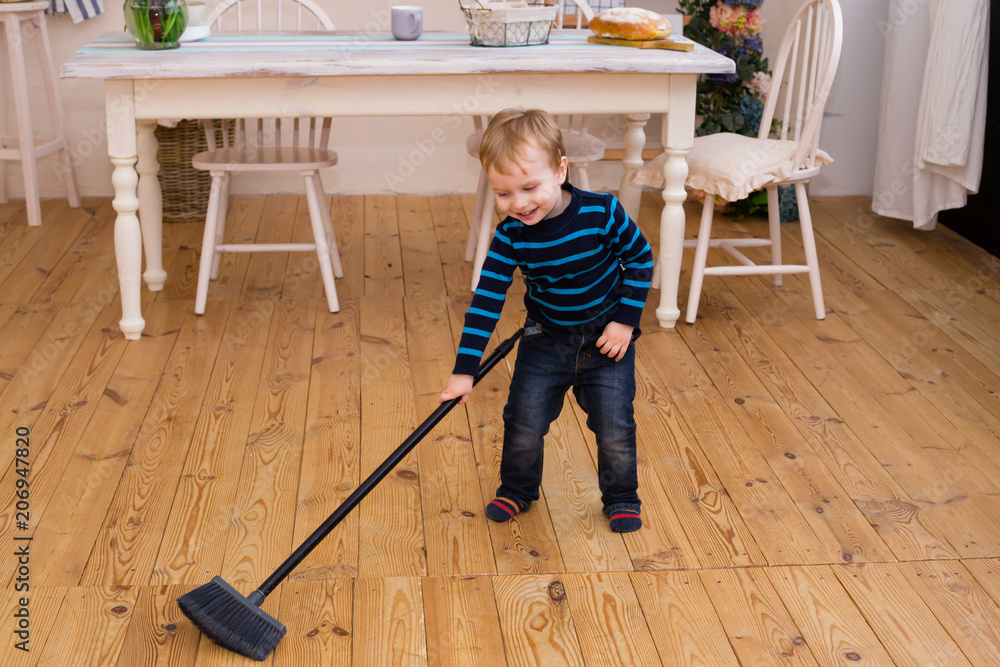 Little blond boy sweeping the floor in the kitchen. Pretty boy 3 yers ...