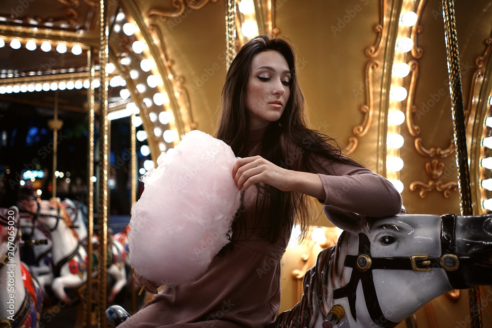 Young beauty model woman posing with old horse carousel in summer park ...