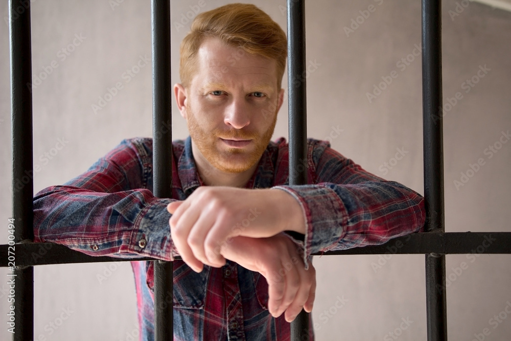 Man with serious expression on his face standing behind bars ...