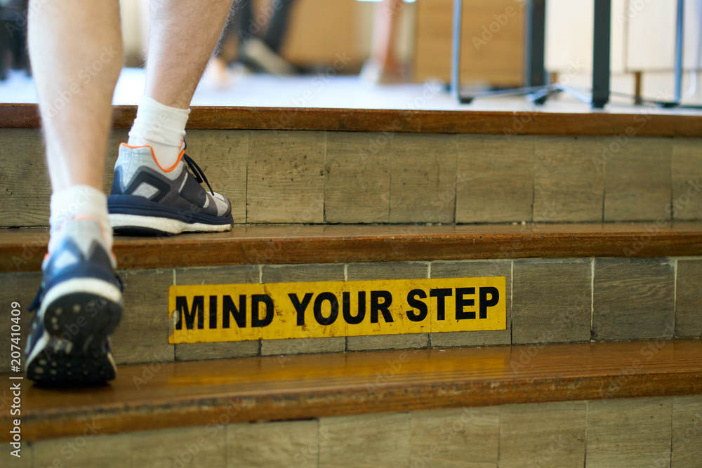 Man walking up the stairs with"Mind your step" safety caution si Stock ...