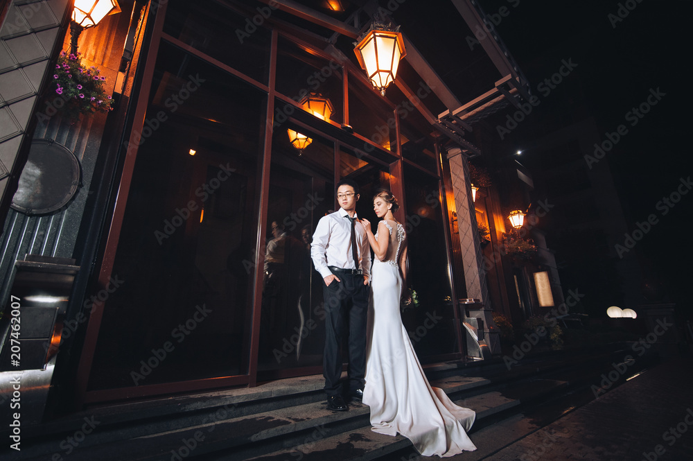 Stylish newlyweds on the background of the hotel. Night wedding walk ...