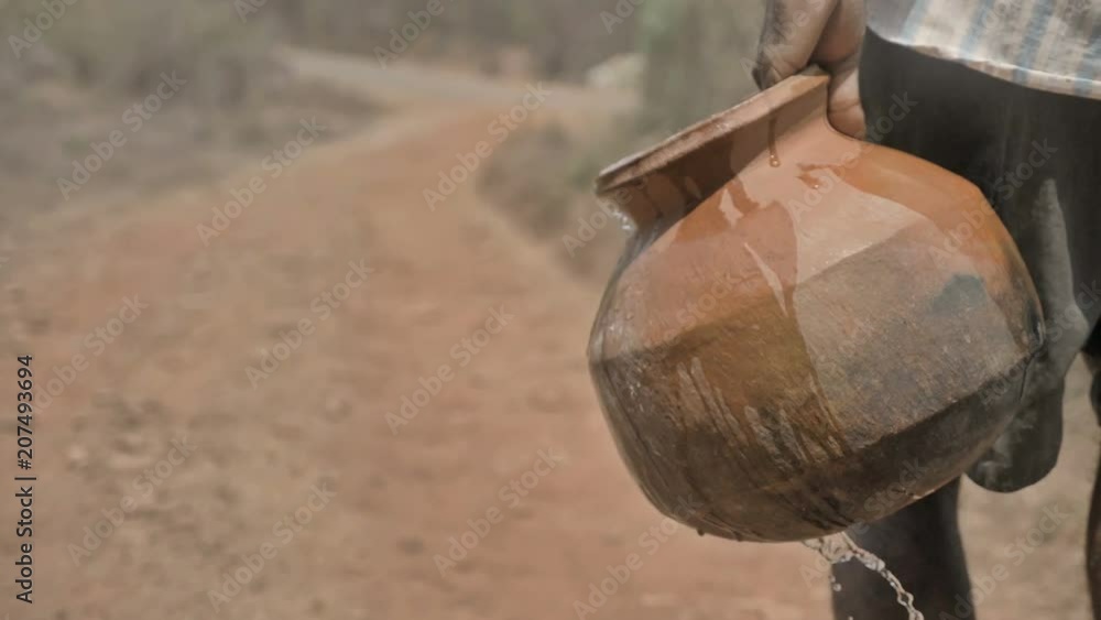 Vídeo do Stock: Water spilling out of a earthen pot of a farmer walking ...