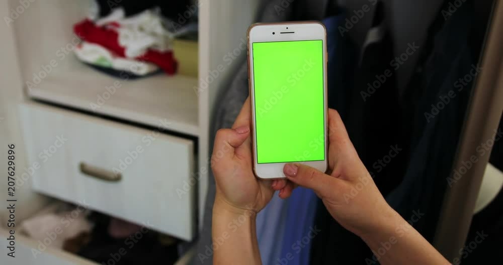 Close up woman hand holding use smart phone with vertical green screen in background of wardrobe ...