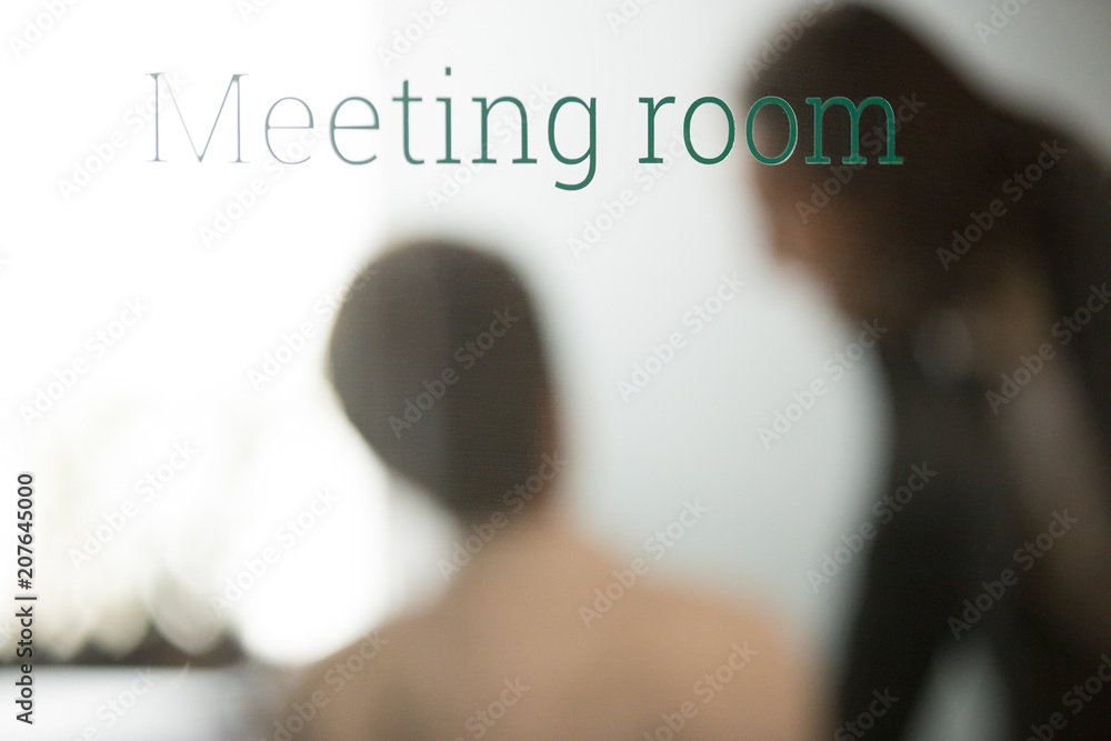Words "Meeting room" written on glass door. Partners talking discussing ...