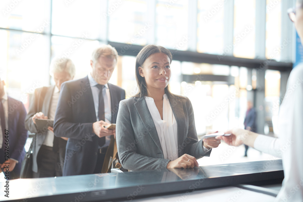 Happy mixed-race businesswoman giving her documents to check-in manager ...