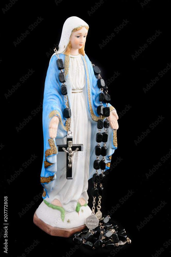 Statue of the Virgin Mary with rosary beads against black background ...