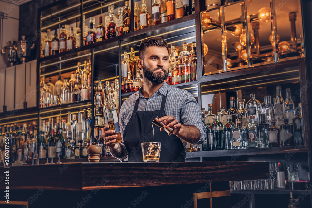 Stylish brutal barman in a shirt and apron makes a cocktail at bar ...