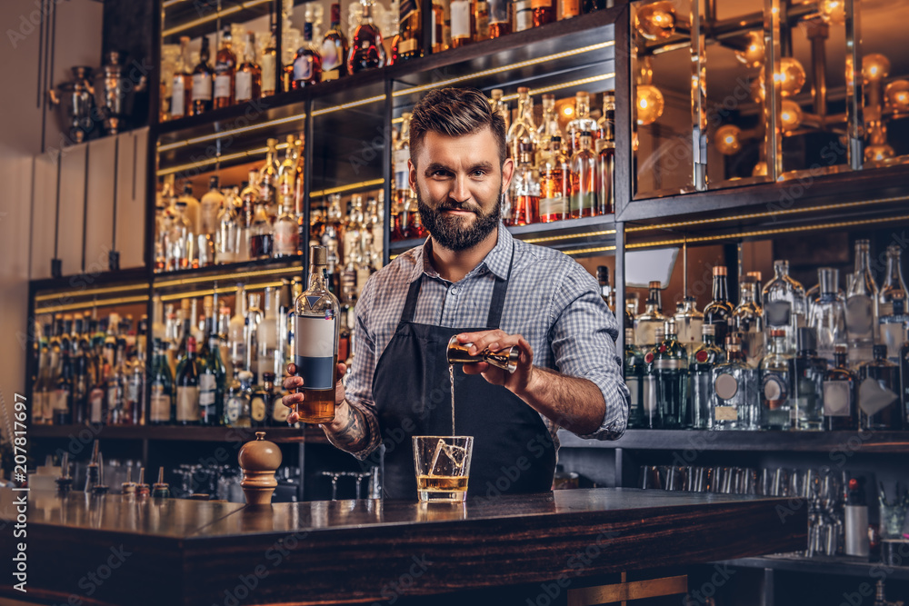 Stylish brutal barman in a shirt and apron makes a cocktail at bar ...
