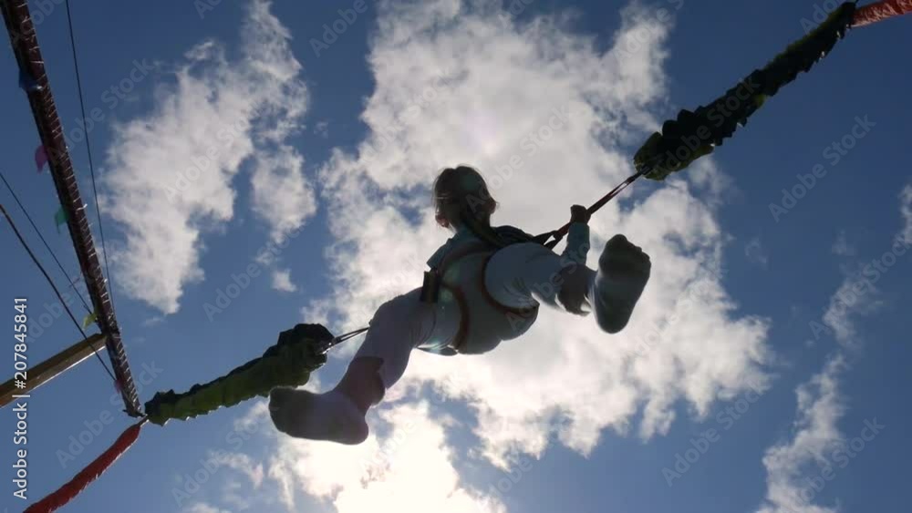 Little girl having fun while bungee jumping up high on trampoline ...