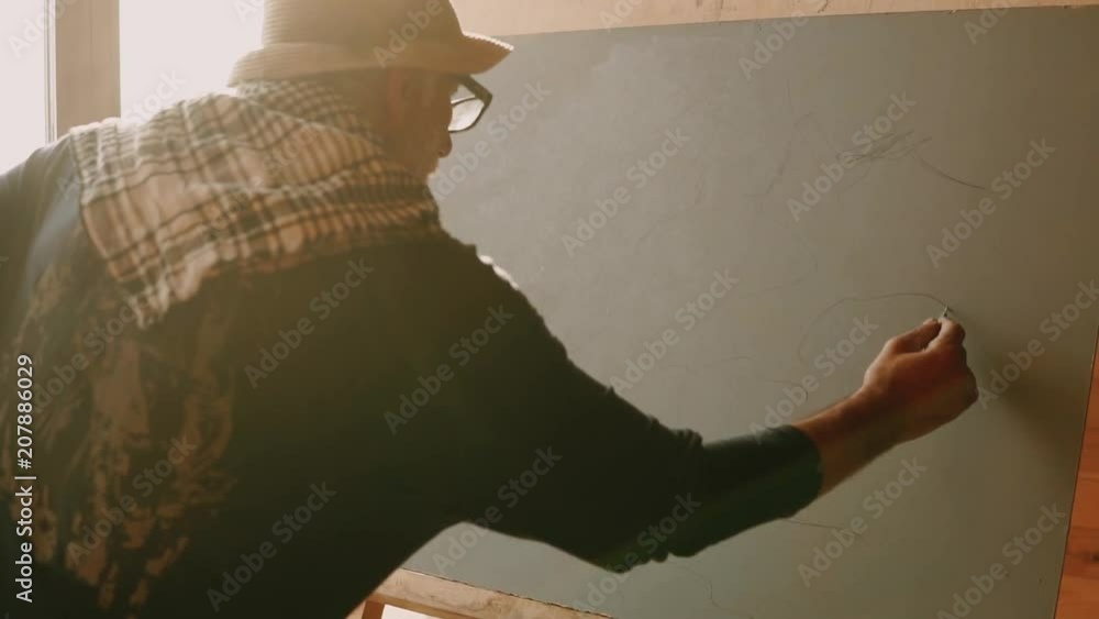 Old man is drawing by pencil on a sheet fixed on easel. He is sketching ...