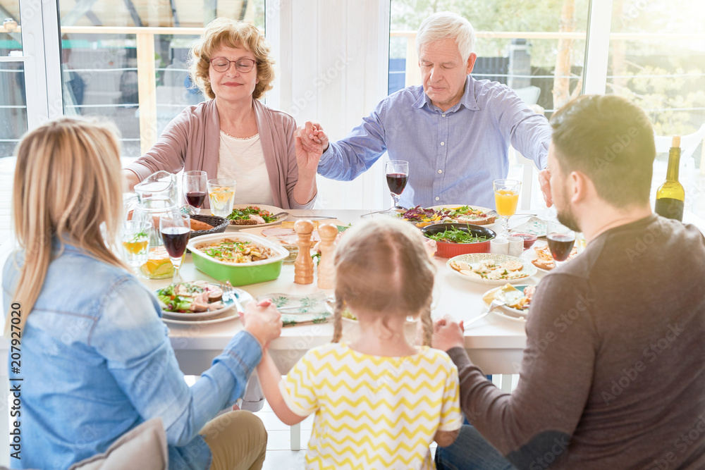 Portrait of big happy family joining hands in prayer at dinner holding ...