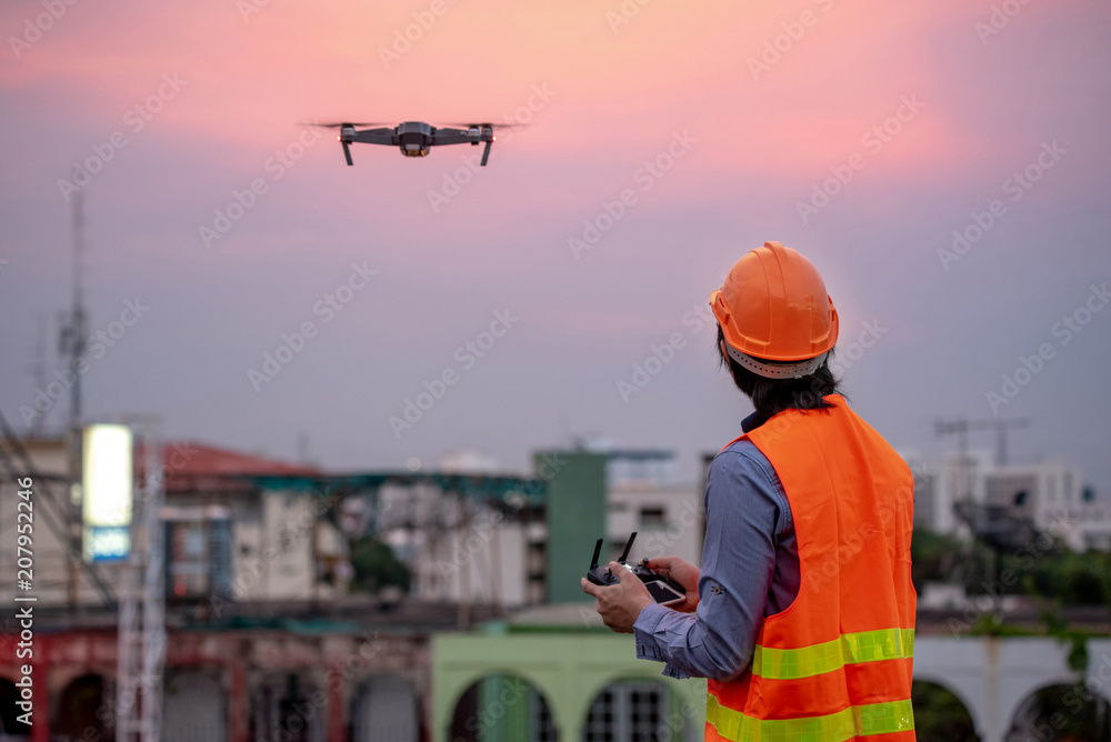 Young Asian engineer flying drone over construction site during sunset ...