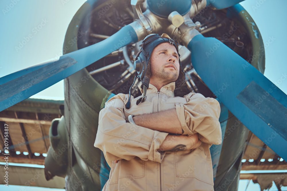 Valiant handsome pilot in a full flight gear standing with crossed arms ...
