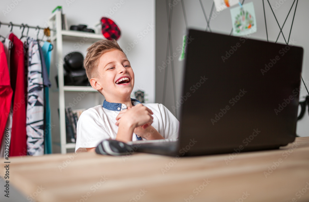 Laughing kid boy using laptop and watching movie in his room at home ...