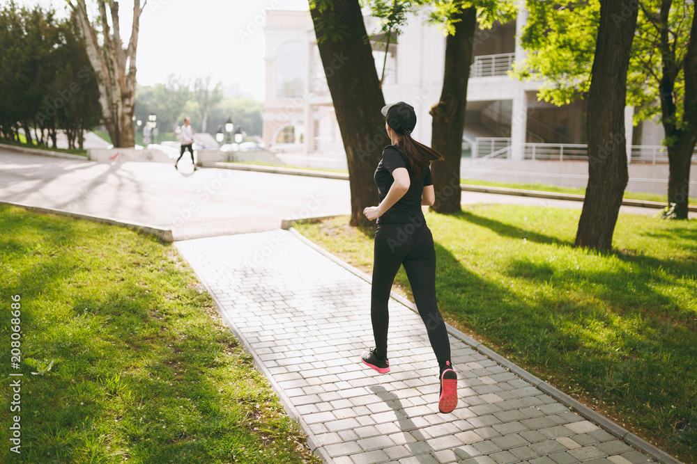 Back view Young athletic brunette girl in black uniform and cap ...