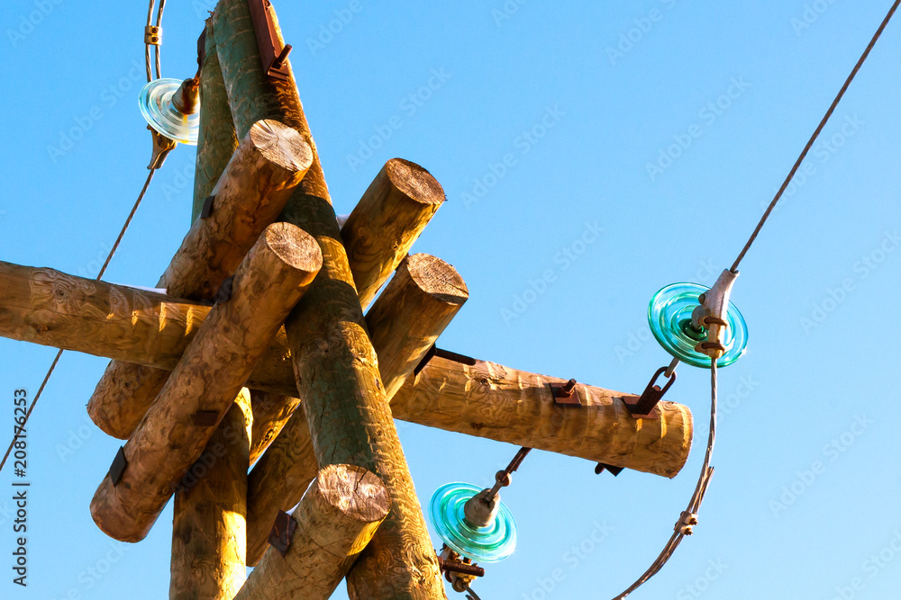 Old fashioned wooden electrical pole with cable line against clean blue ...